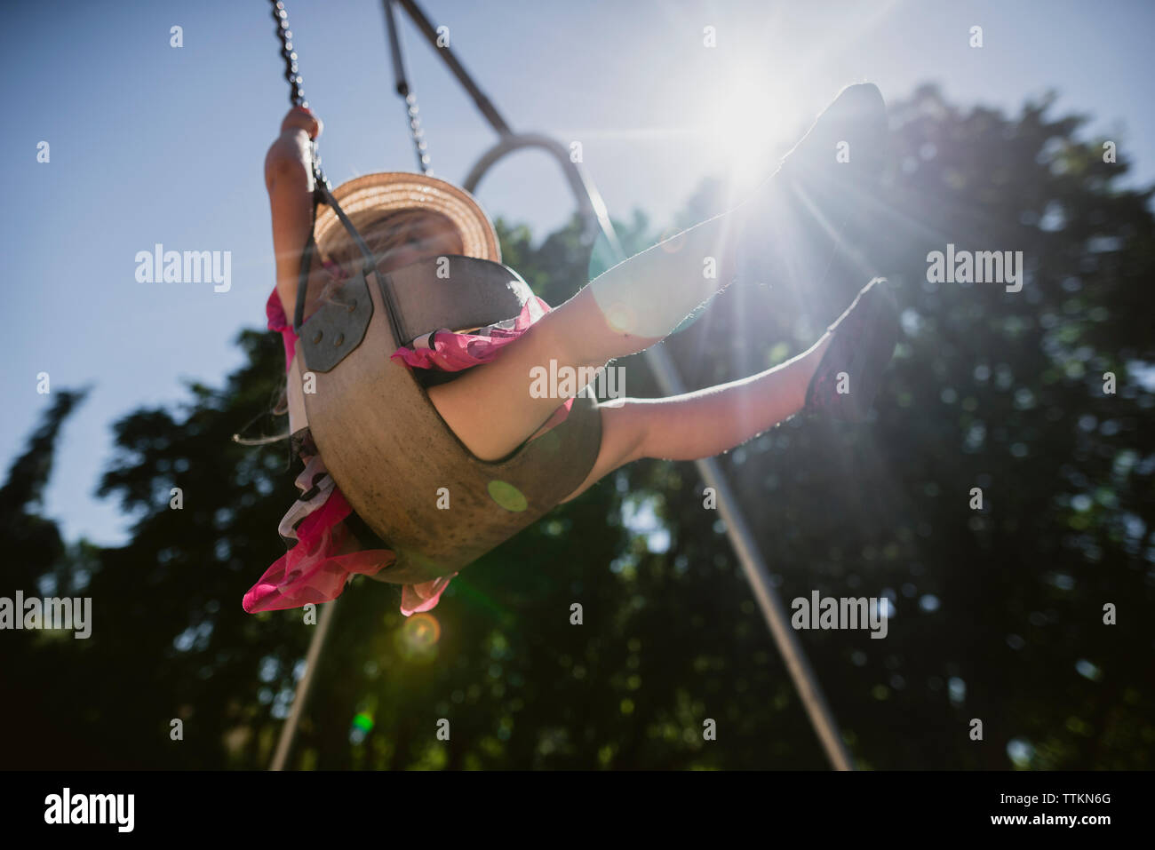 Low angle view of playful girl swinging on swing at playground during ...