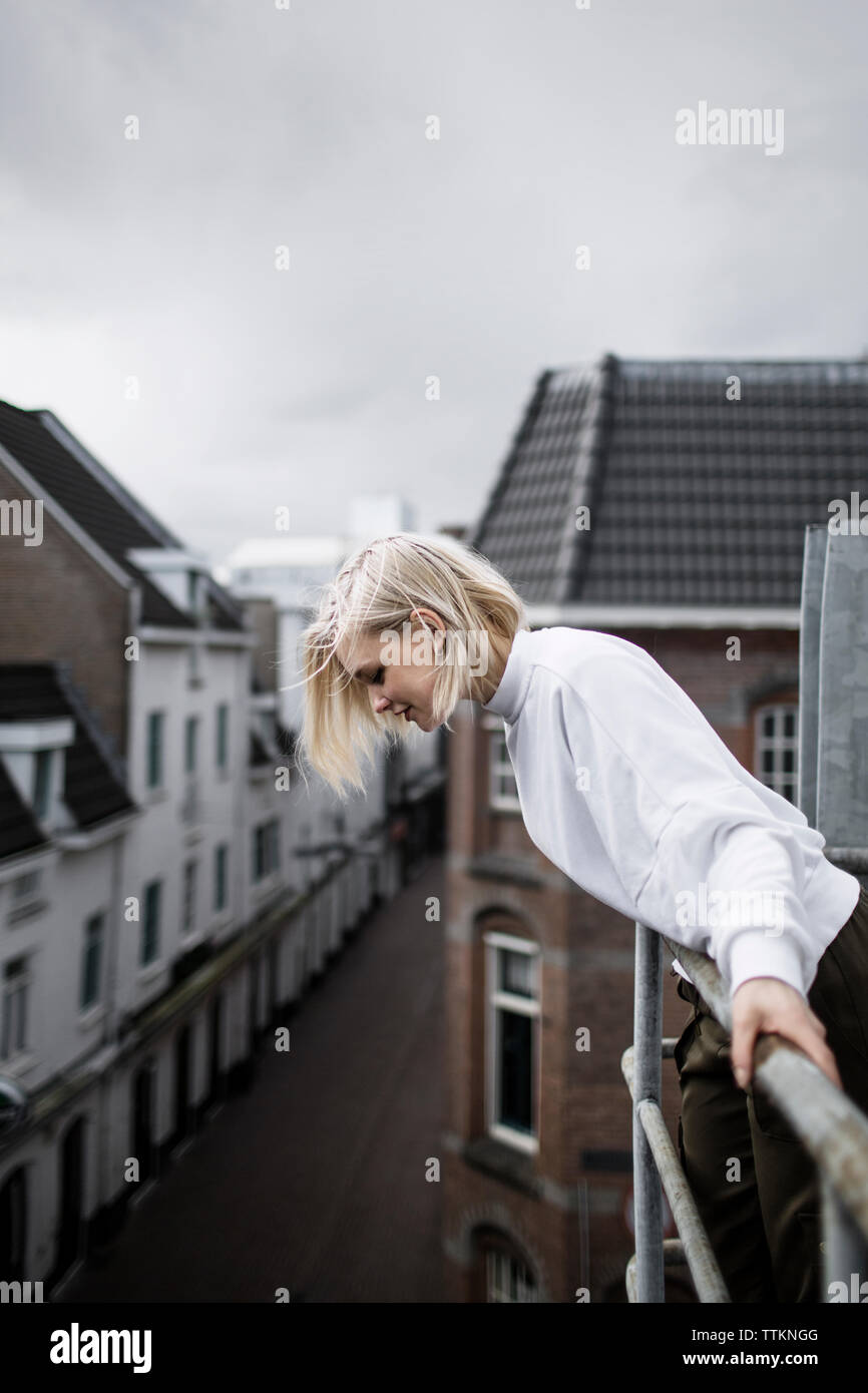 Side view of woman looking down while leaning on balcony railing Stock ...