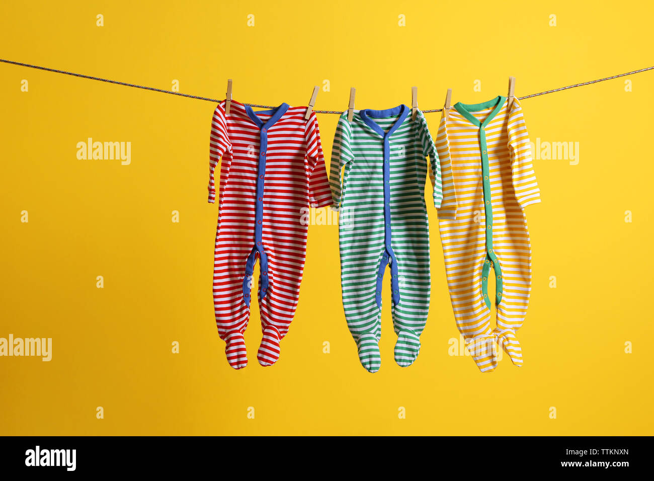Baby clothes hanging on rope on yellow background Stock Photo - Alamy