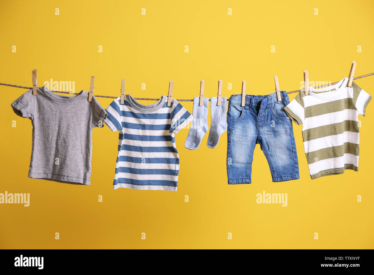 Baby clothes hanging on rope on yellow background Stock Photo - Alamy