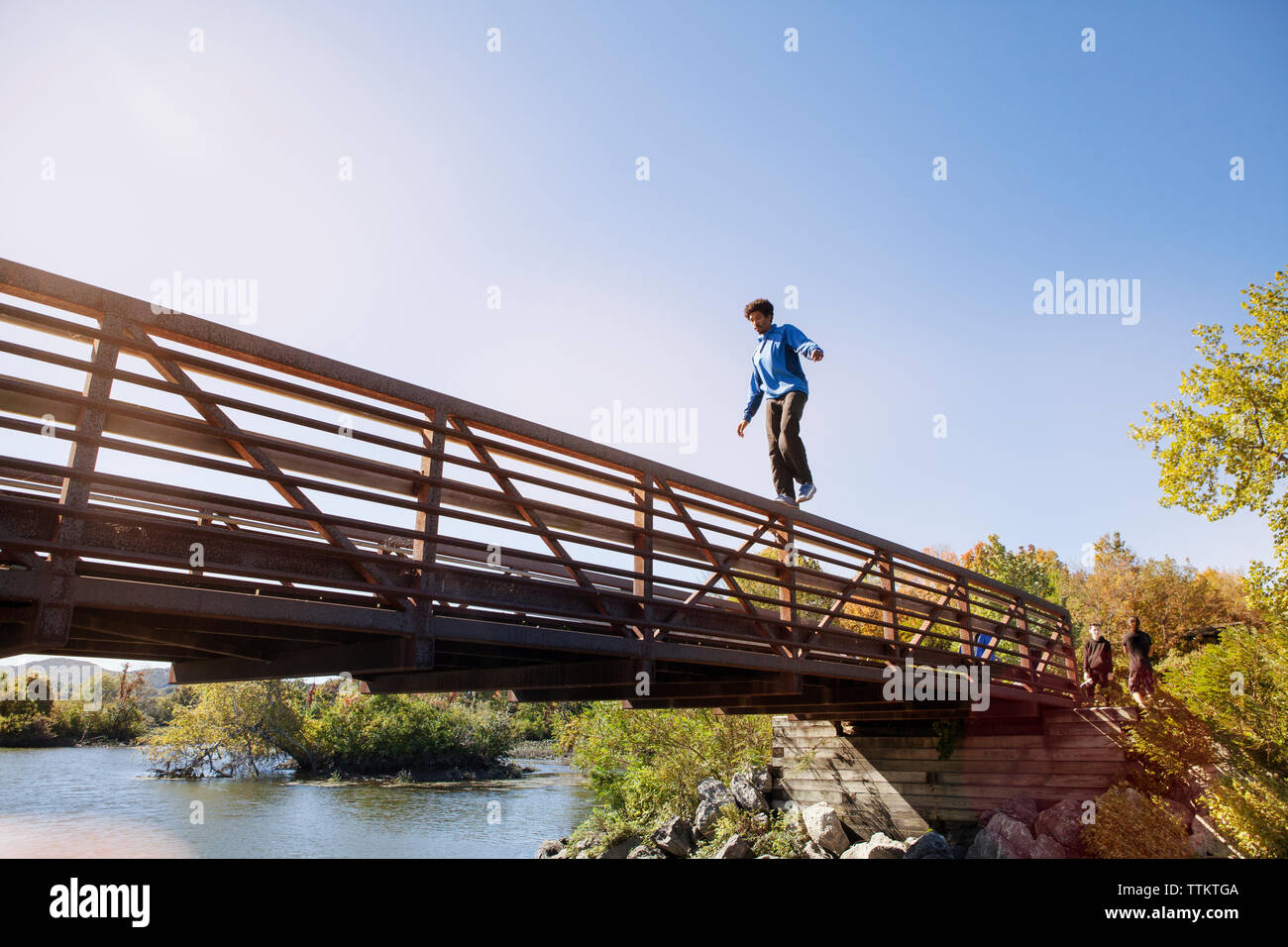 Low angle view of man walking on bridge railing against clear blue sky ...