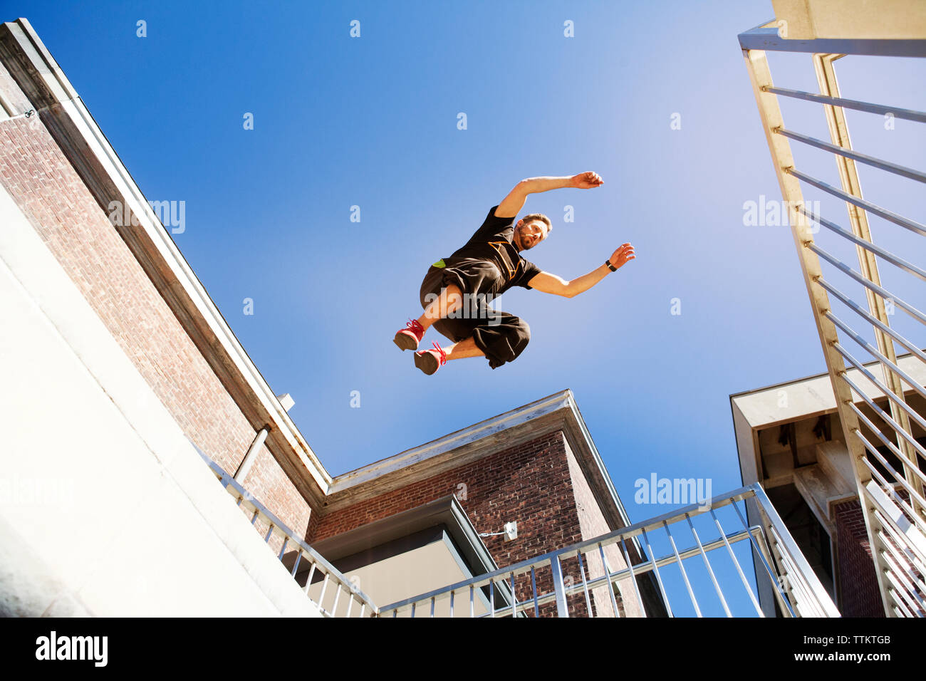 Low angle view of man jumping on buildings against clear blue sky Stock ...