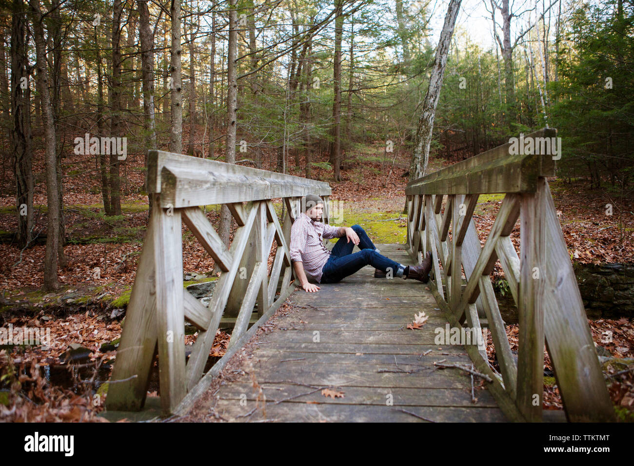 Side view of thoughtful man sitting on footbridge in forest Stock Photo ...