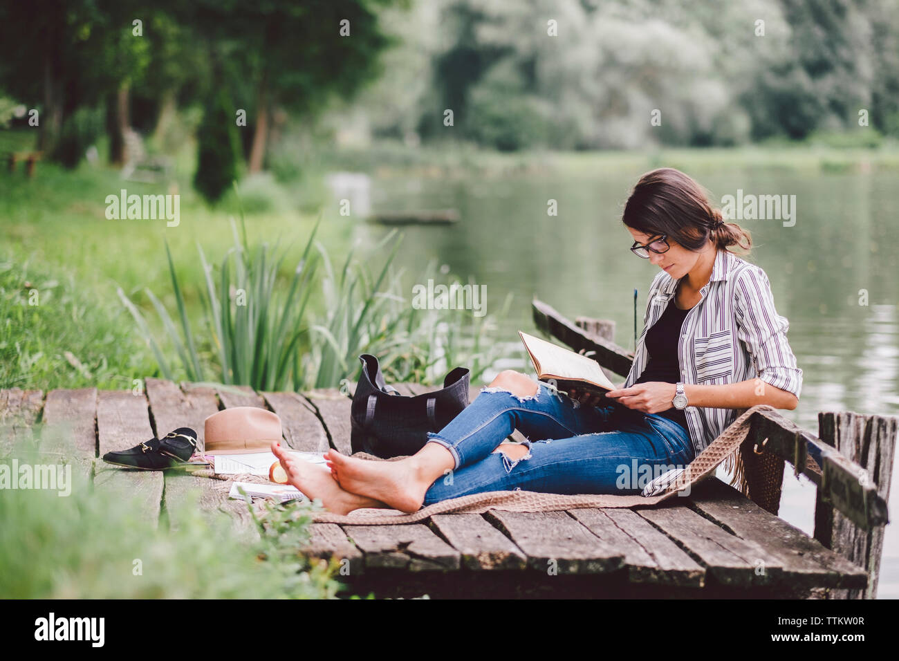 Woman reading book while sitting on pier against lake in forest Stock ...