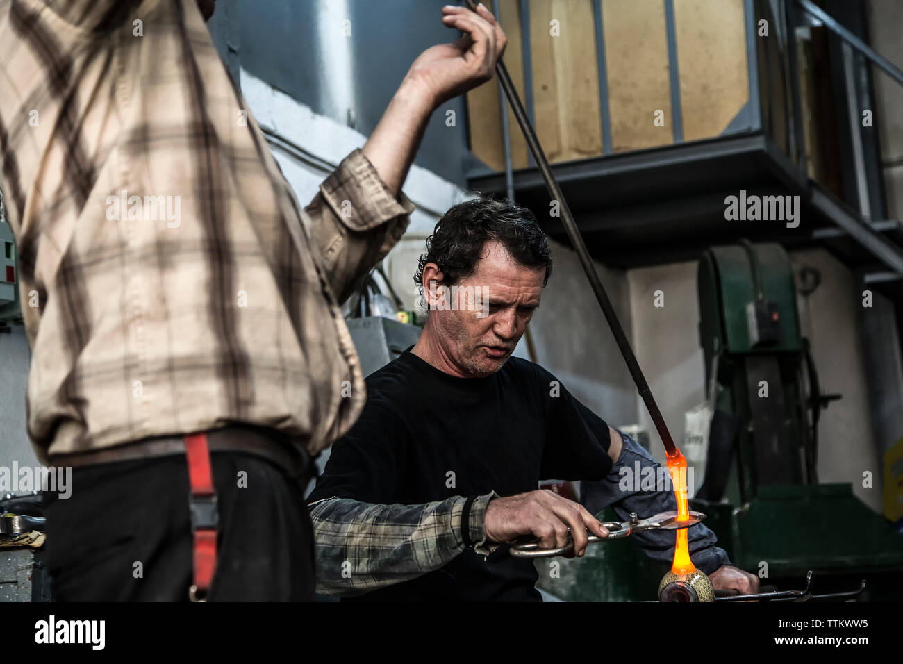 Glass blower cutting molten glass with scissors in workshop with ...