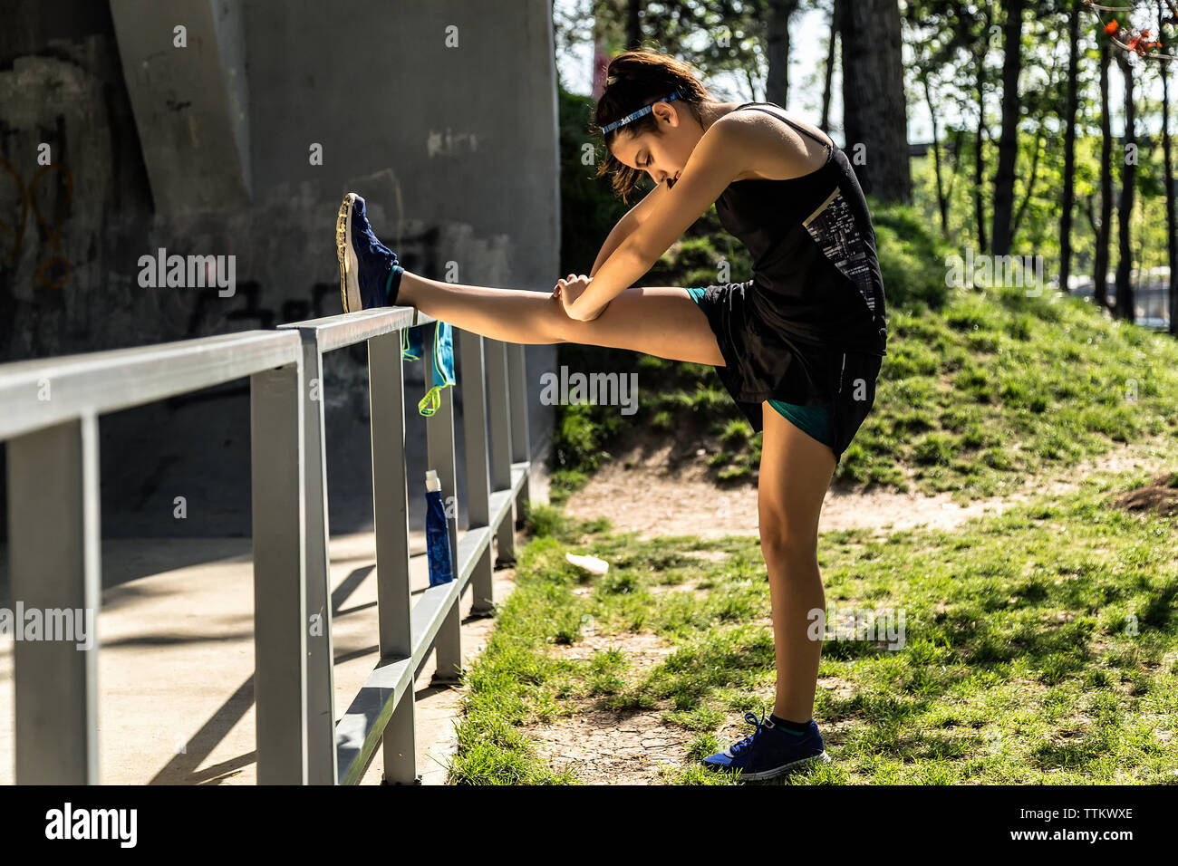 Side view of female athlete stretching leg on railing at park Stock ...
