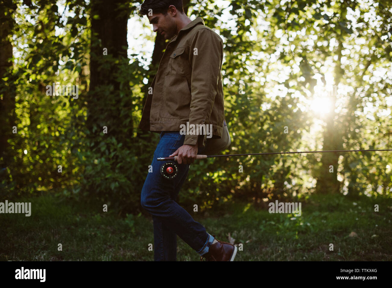 Side view of man holding fishing rod while walking in forest Stock ...