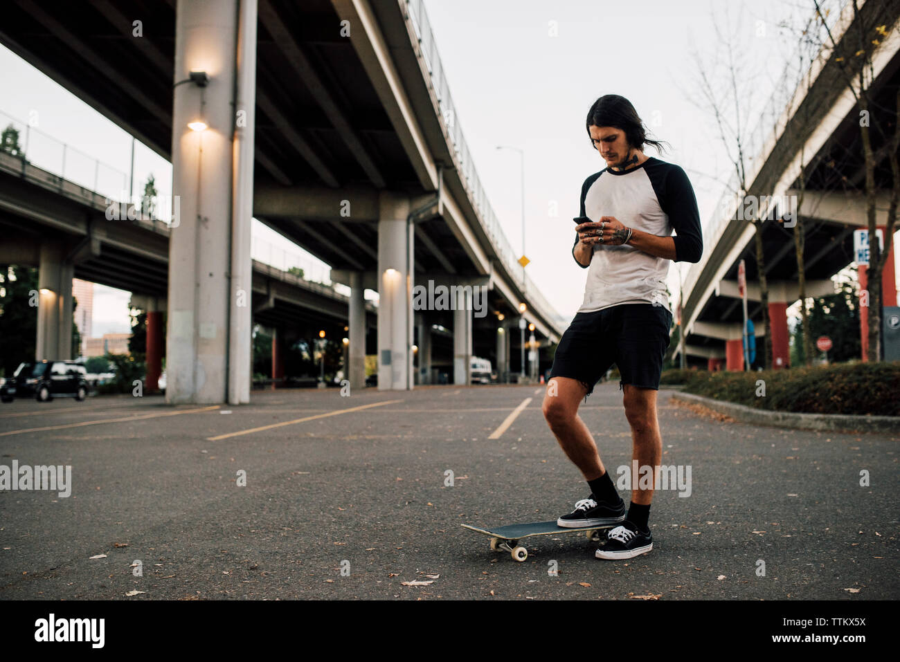 Man using mobile phone while standing with skateboard on street Stock ...