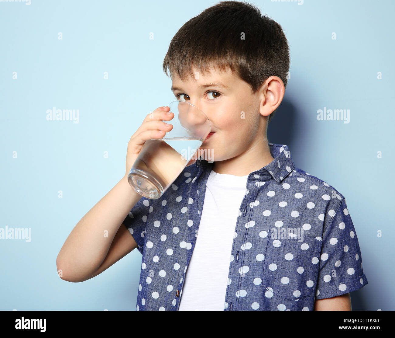 Cute boy drinking water on light background Stock Photo - Alamy
