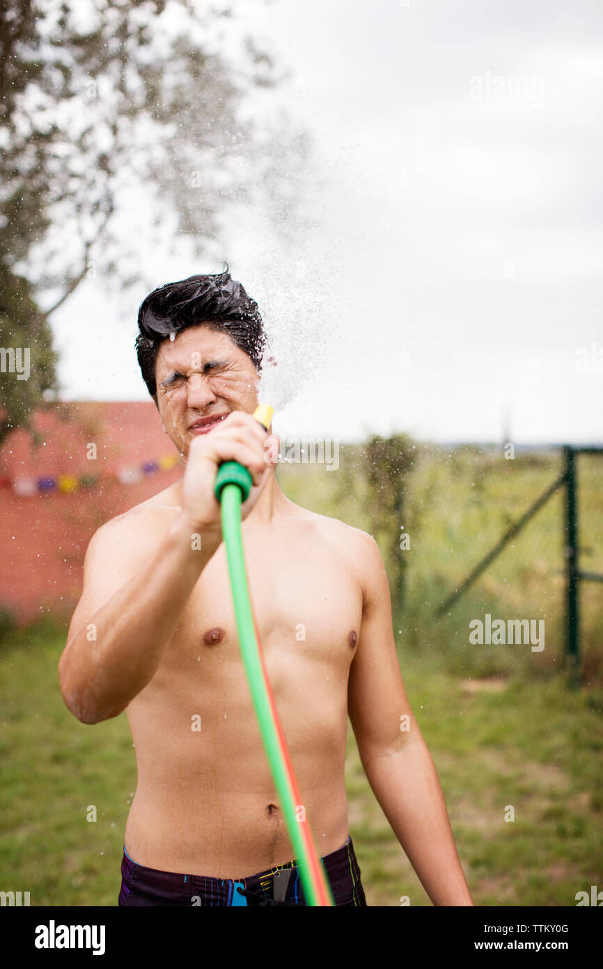 Shirtless man spraying water on face at yard Stock Photo - Alamy