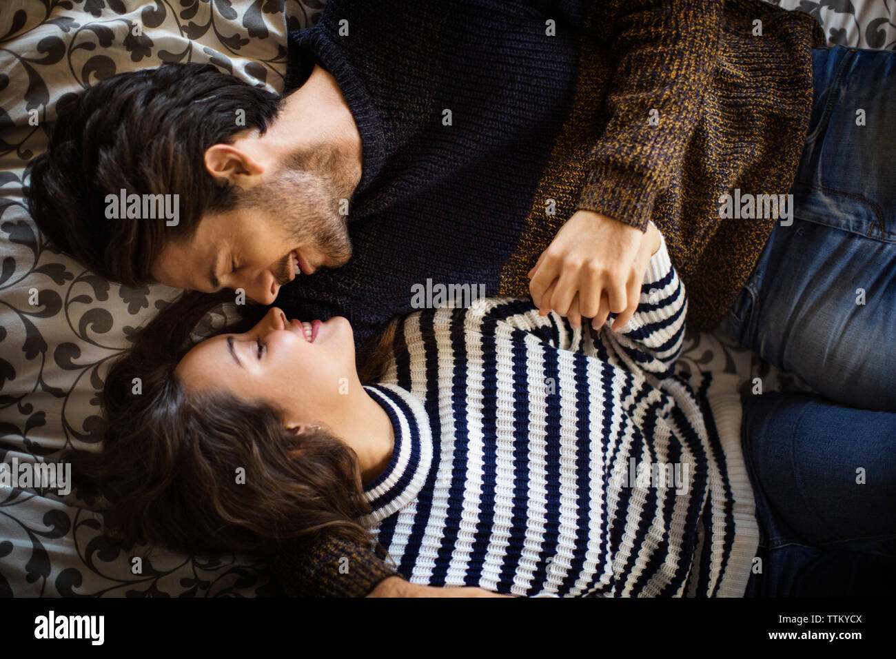 High angle view of couple lying with holding hands on alcove window ...