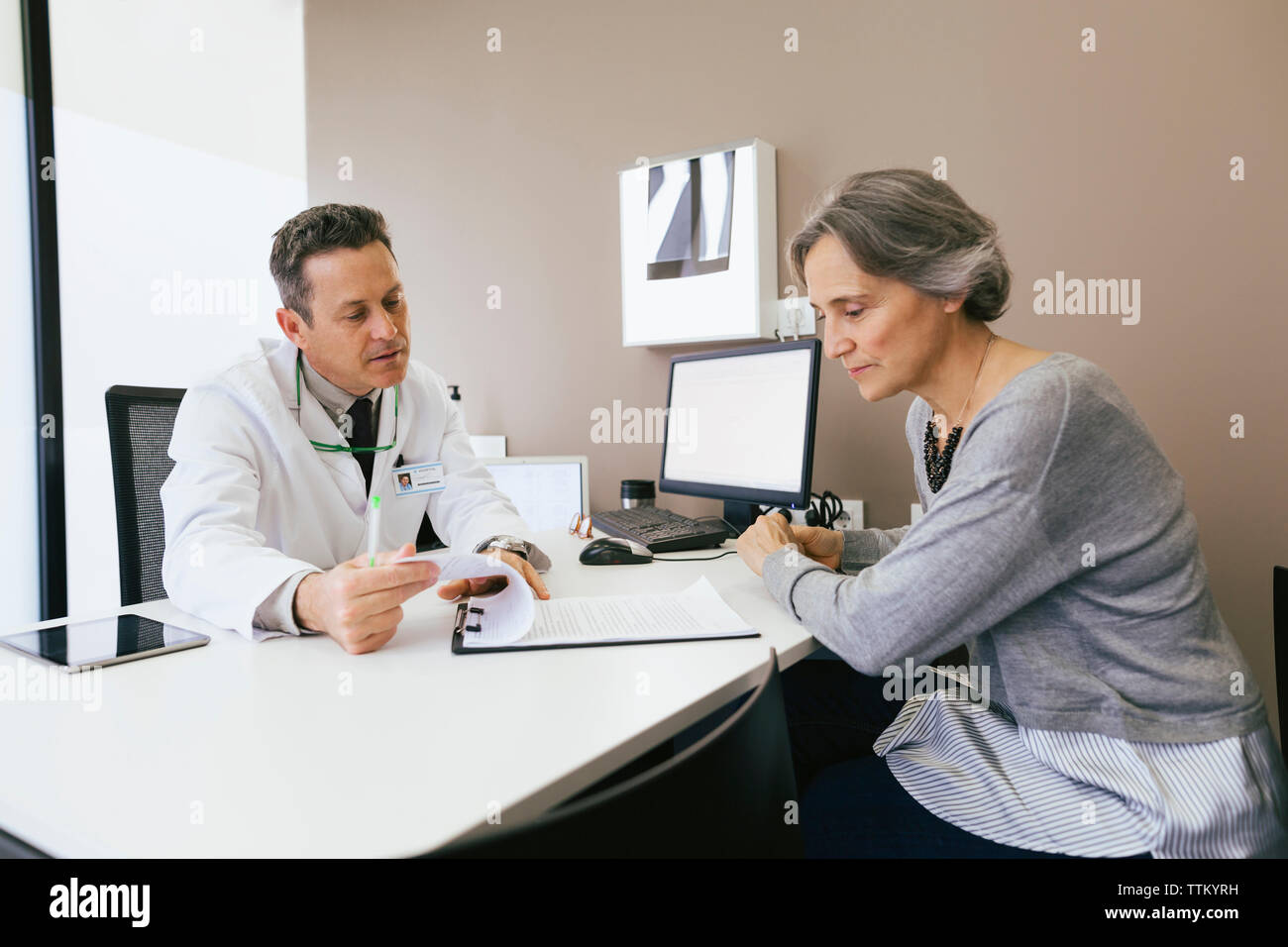 Doctor discussing with patient while sitting against wall at hospital ...