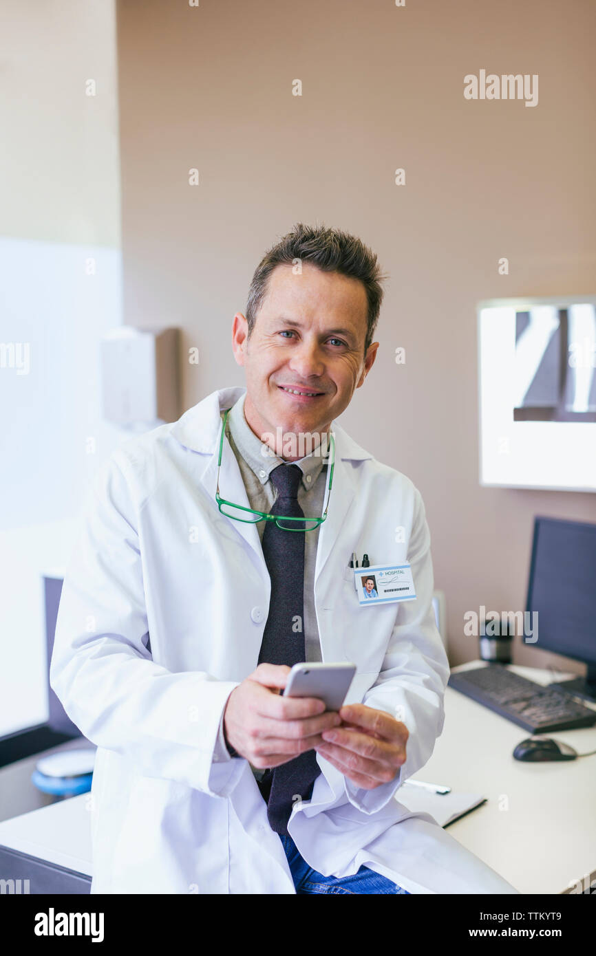 Portrait of smiling doctor holding smart phone while sitting at ...