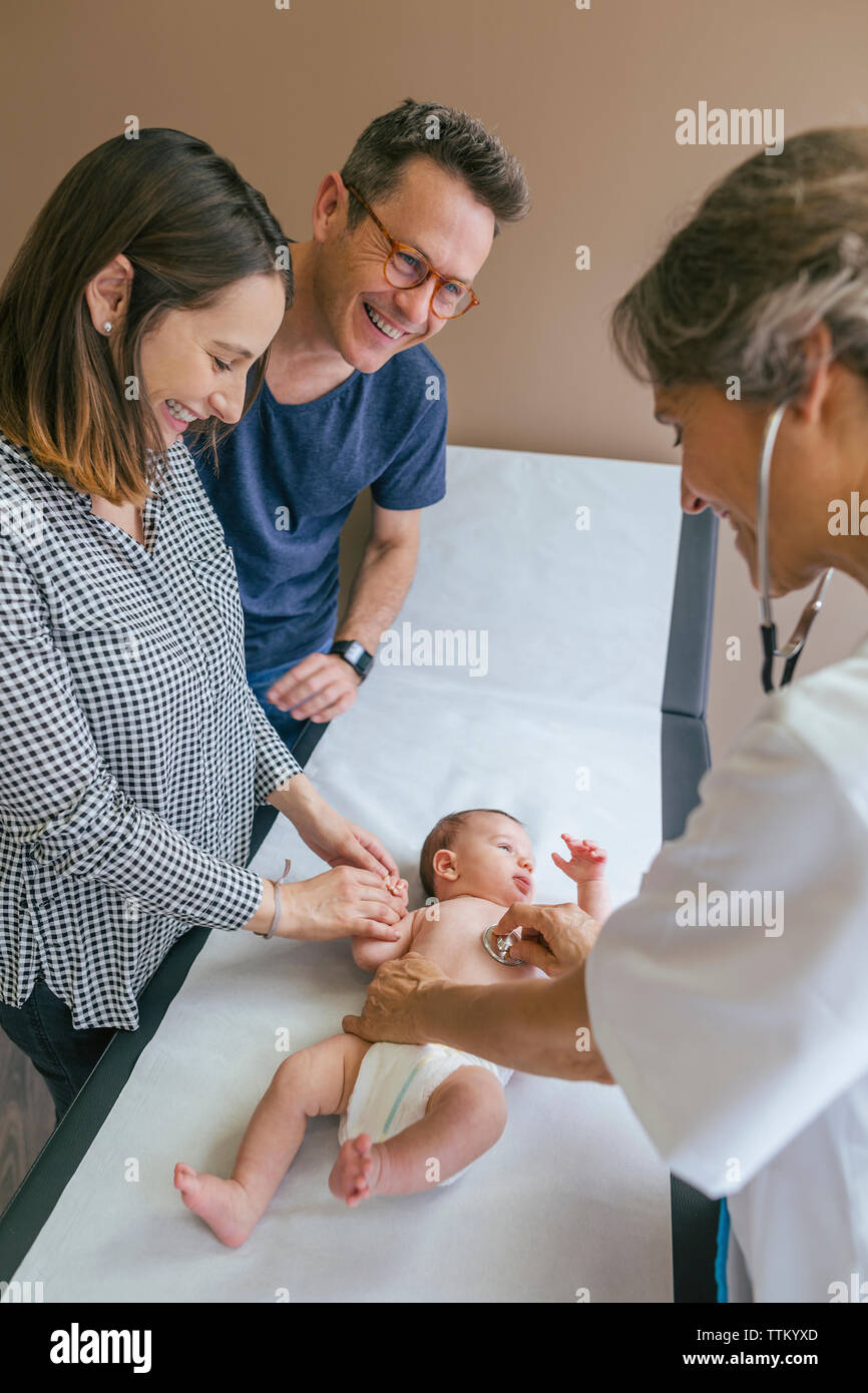 Happy parents looking at doctor examining baby boy in medical clinic ...