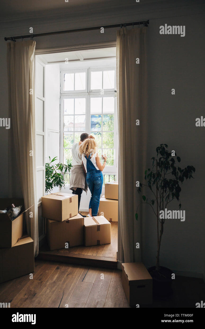Rear view of couple looking through window while standing in new house ...