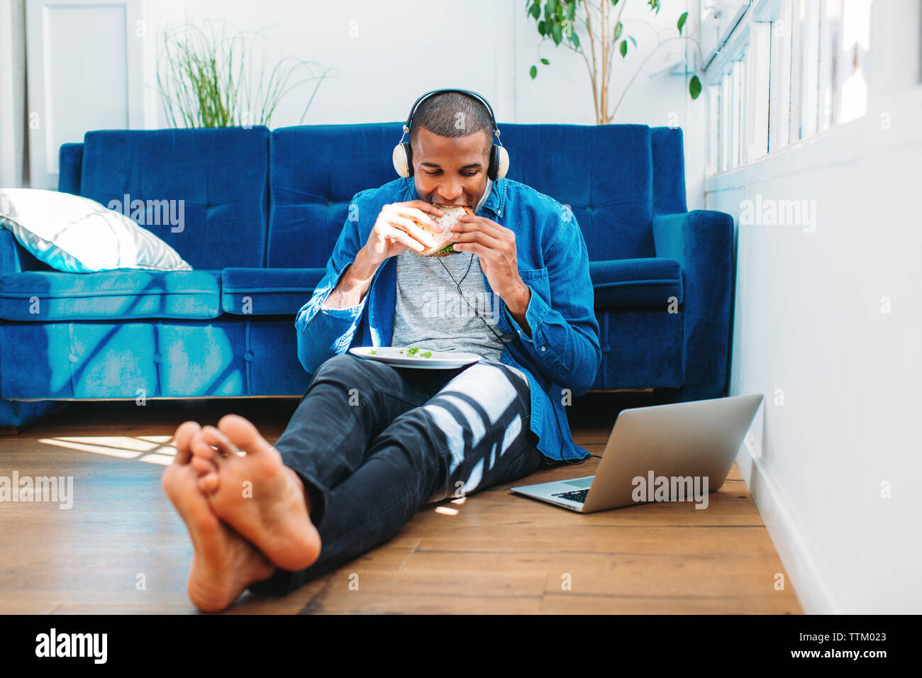Man eating sandwich while listening music through laptop computer by ...