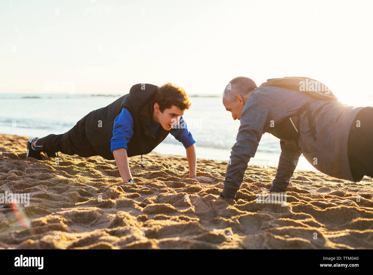 Determined father and son doing push-ups together against clear sky at ...