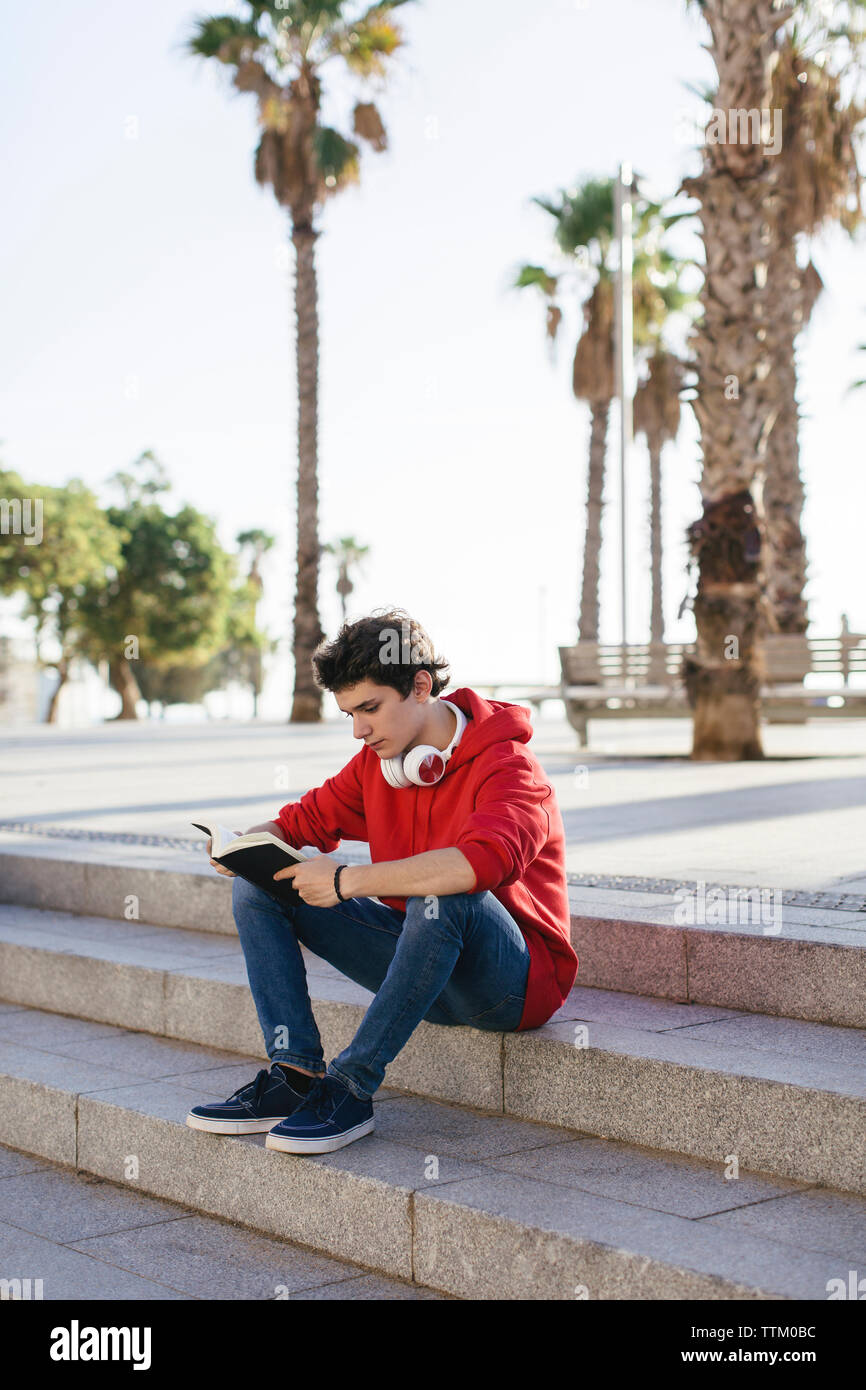 Serious teenage boy reading book while sitting on steps in city Stock ...