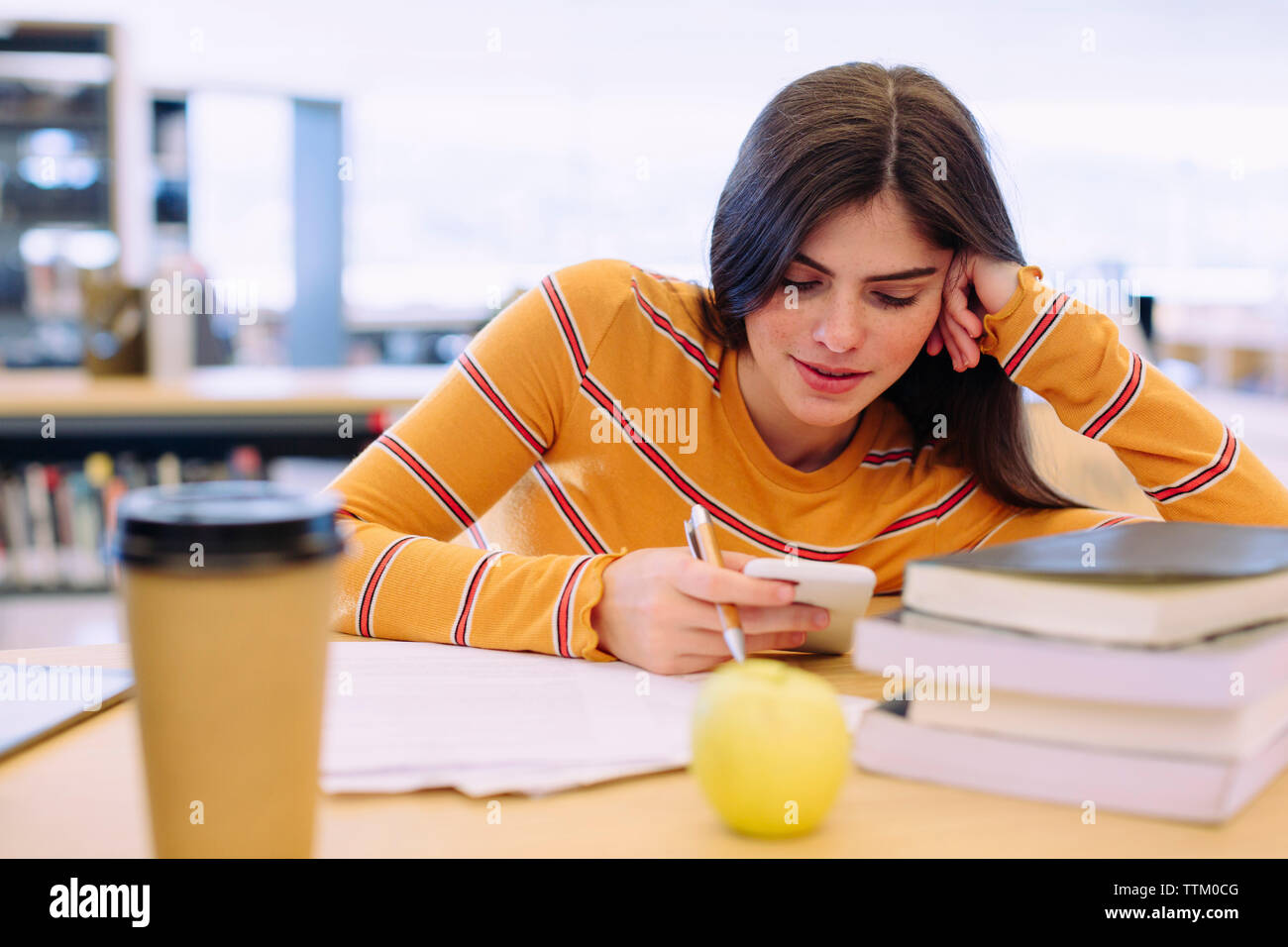 Woman using mobile phone while studying in library Stock Photo - Alamy
