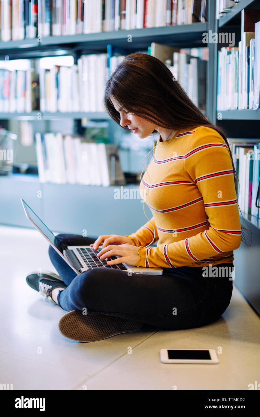Side view of woman using laptop computer while sitting on floor in ...