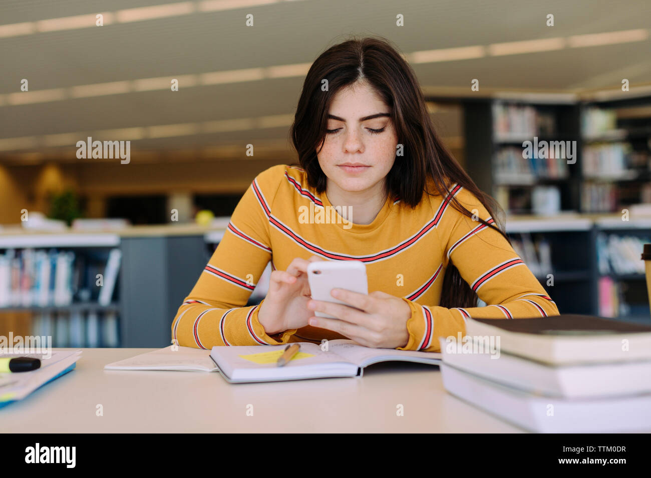 Woman using mobile phone while studying in library Stock Photo - Alamy