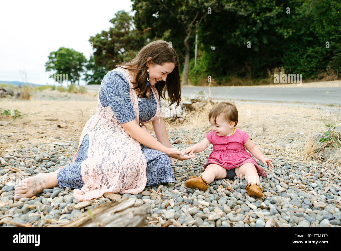 Happy mother playing with cute daughter while sitting on pebbles at ...