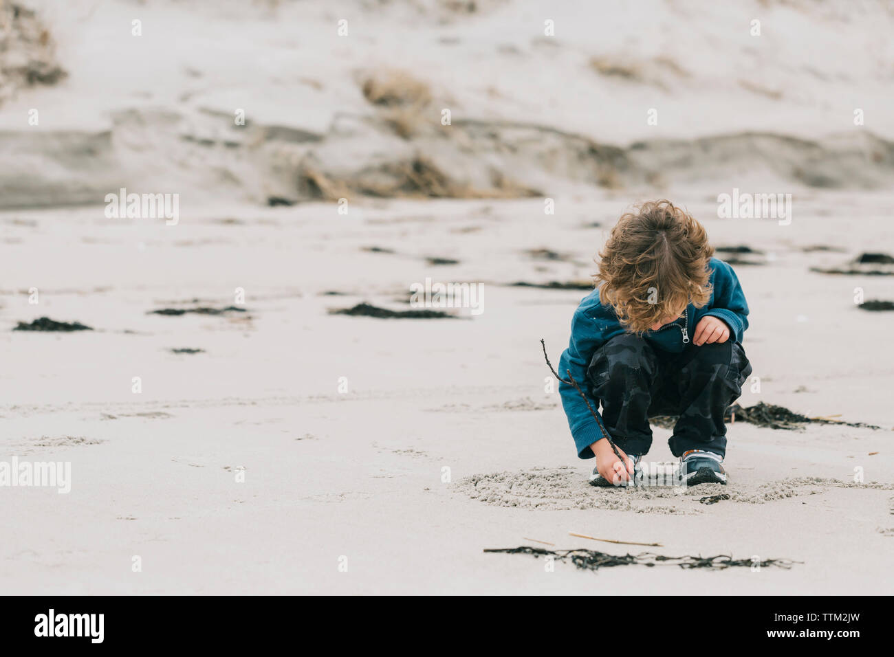 Boy writing on sand while crouching at beach Stock Photo - Alamy