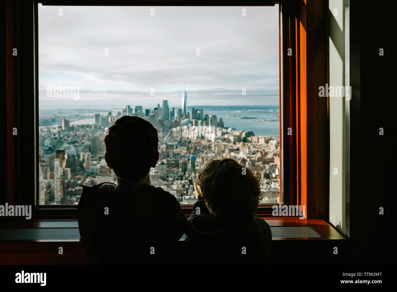 Rear view of brothers looking at cityscape through window at home Stock ...
