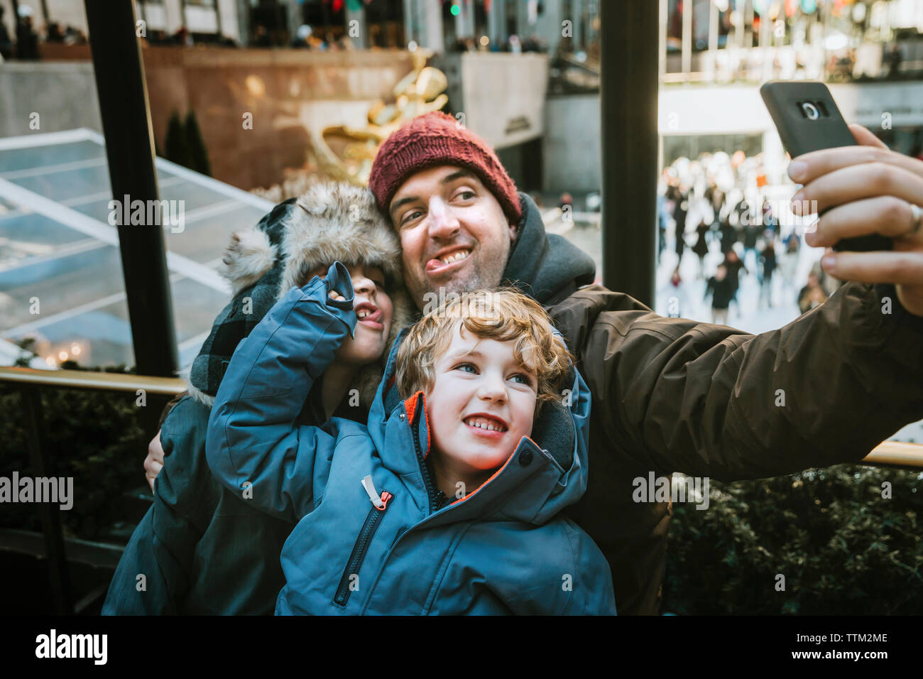 Happy father with sons making face while taking selfie against window ...