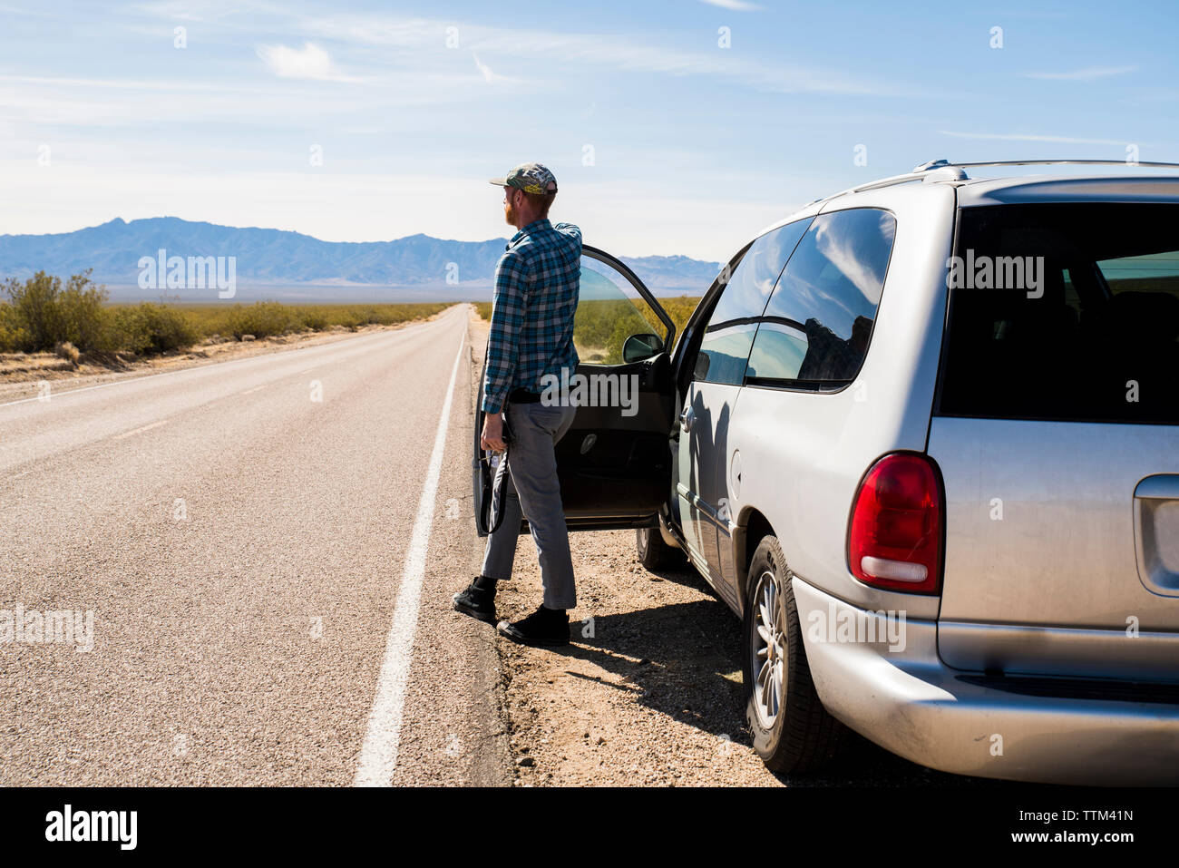 Full length of man standing by car on road at desert during sunny day ...