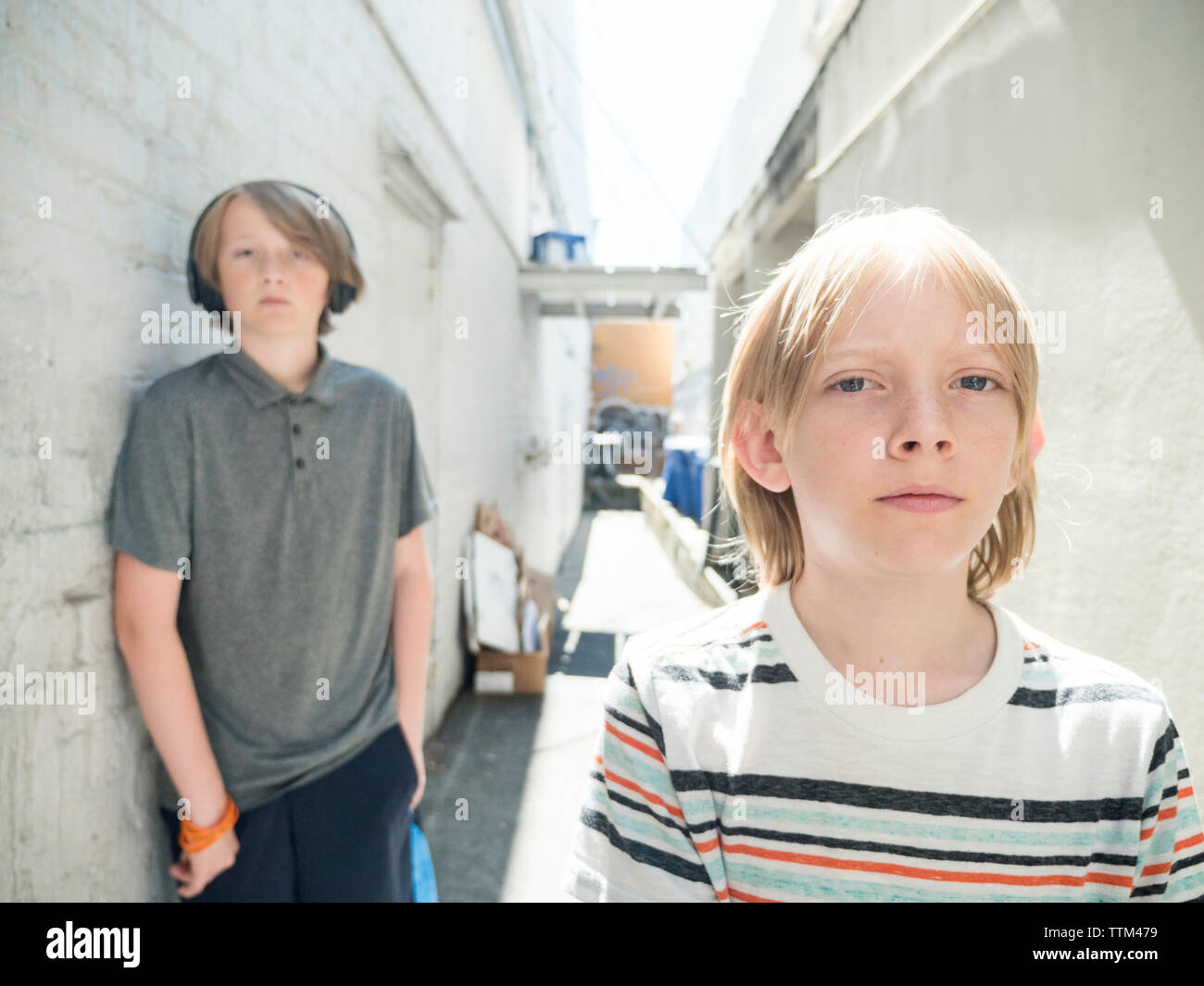 Portrait of brothers standing amidst wall at alley during sunny day ...