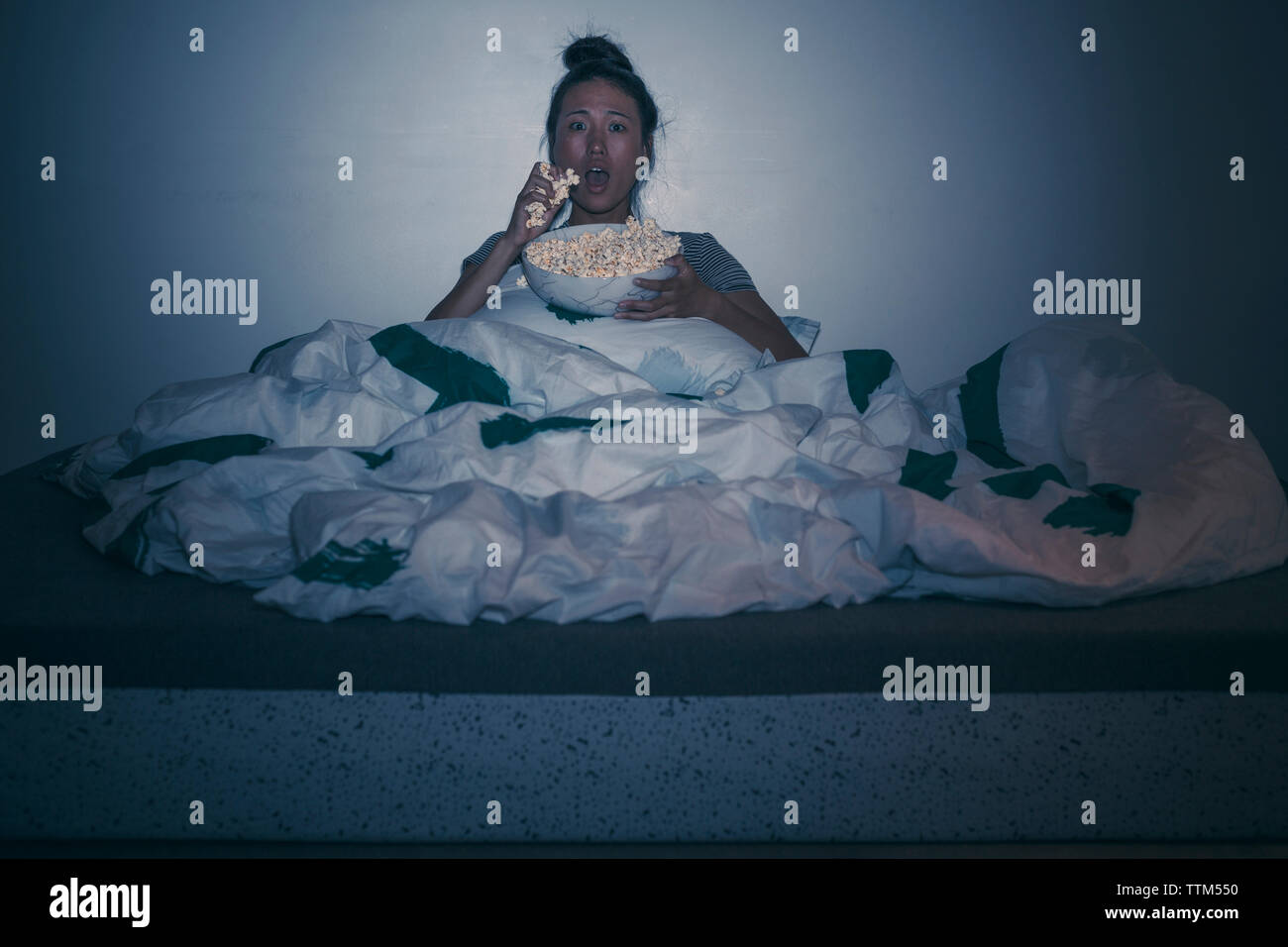 Woman eating popcorn while sitting on bed at home Stock Photo - Alamy