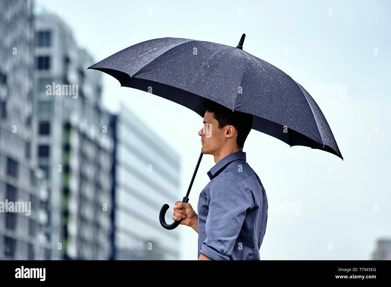 Side view of young businessman with umbrella standing against buildings ...