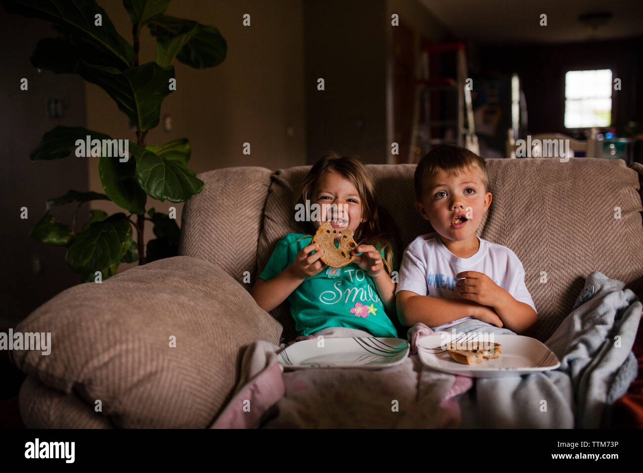 Happy siblings eating bread on sofa Stock Photo - Alamy