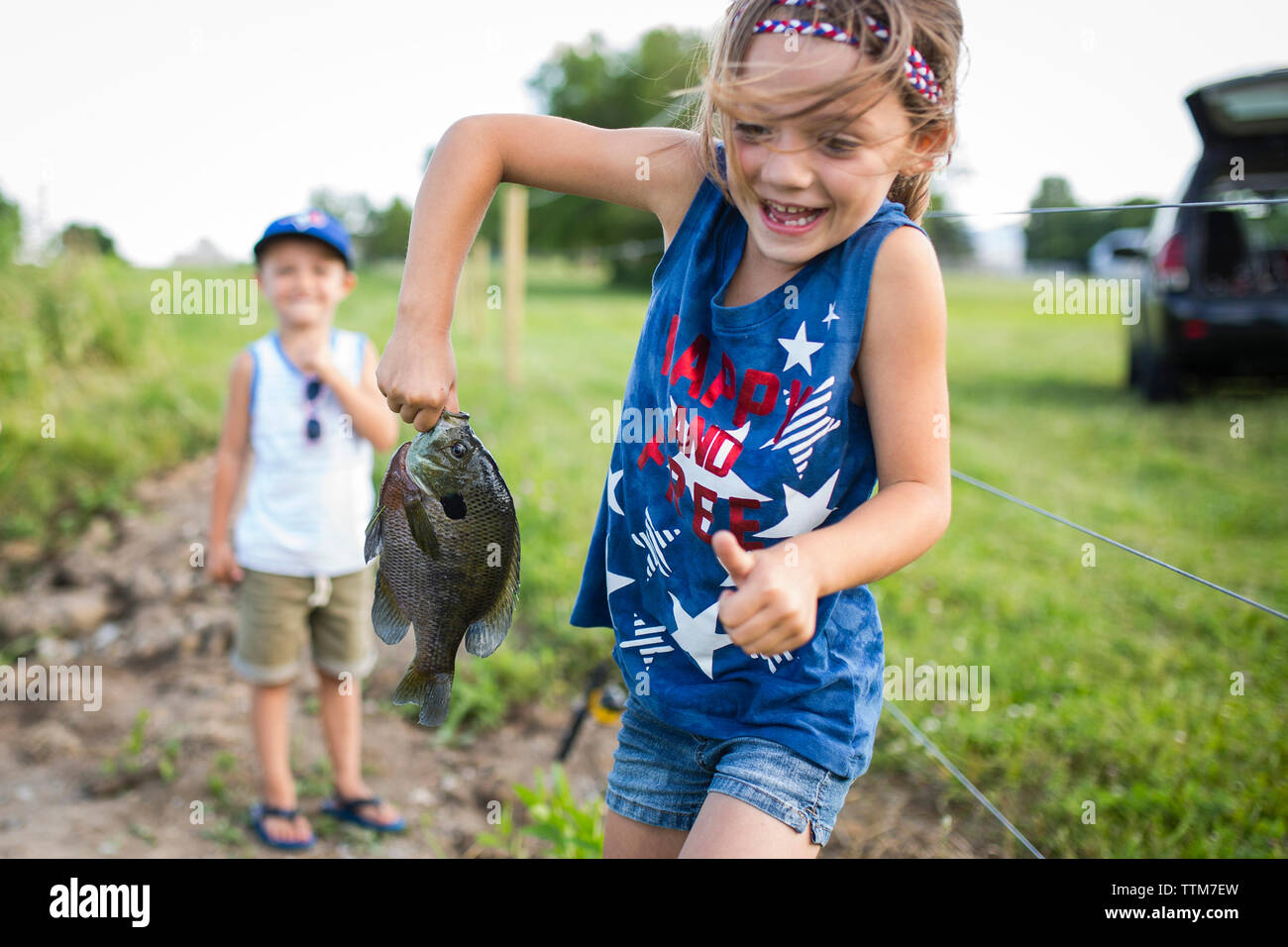 Playful sister with caught fish while brother standing in background ...