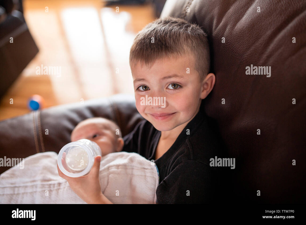 Portrait of boy feeding milk to brother from baby bottle while sitting ...