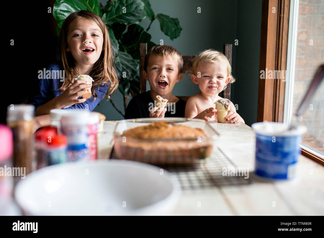 Three happy siblings enjoying a baked treat together indoors Stock ...
