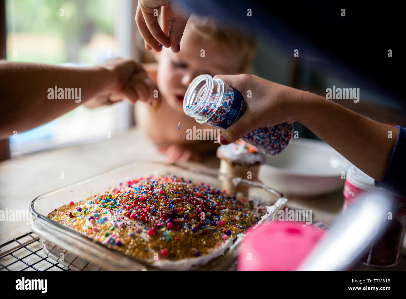 Three siblings decorating cake with lots of sprinkles Stock Photo - Alamy