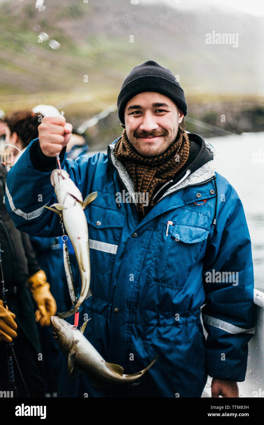 Portrait of smiling man holding fishes while standing by railing Stock ...