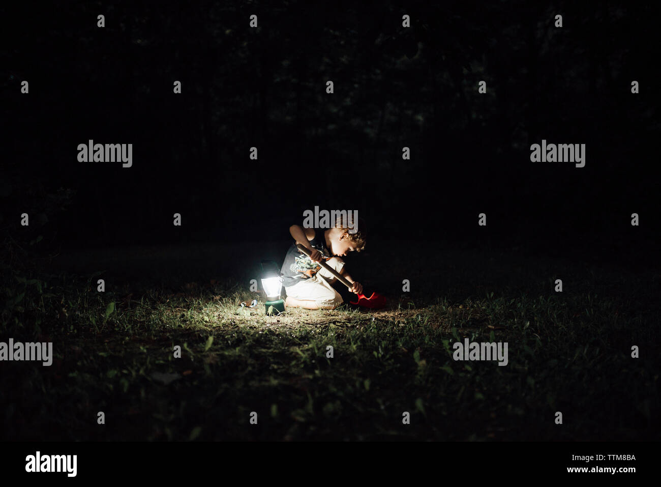 Boy digging soil with shovel at yard by illuminated lantern during ...