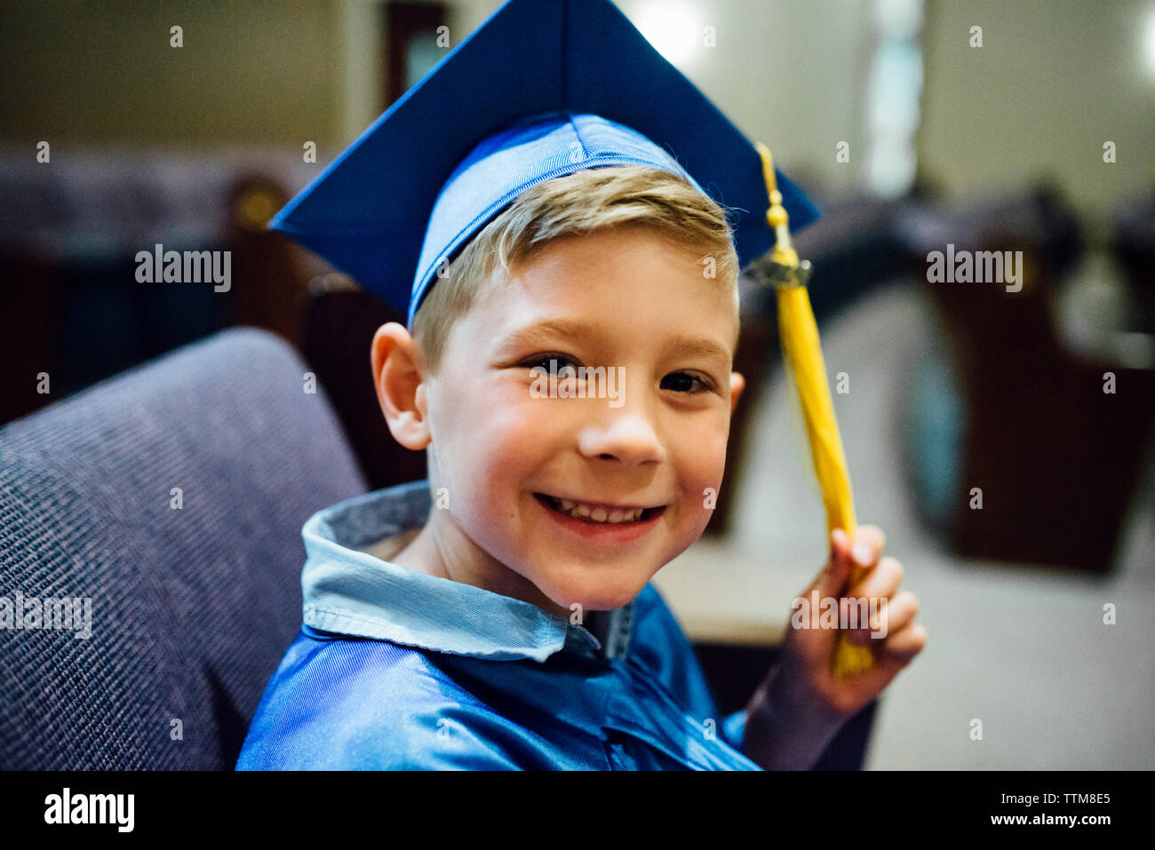Portrait of happy boy in graduation gown siting on chair Stock Photo ...