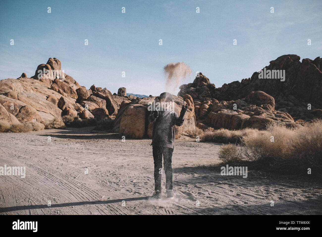 Playful boy throwing sand while standing against rock formations at ...