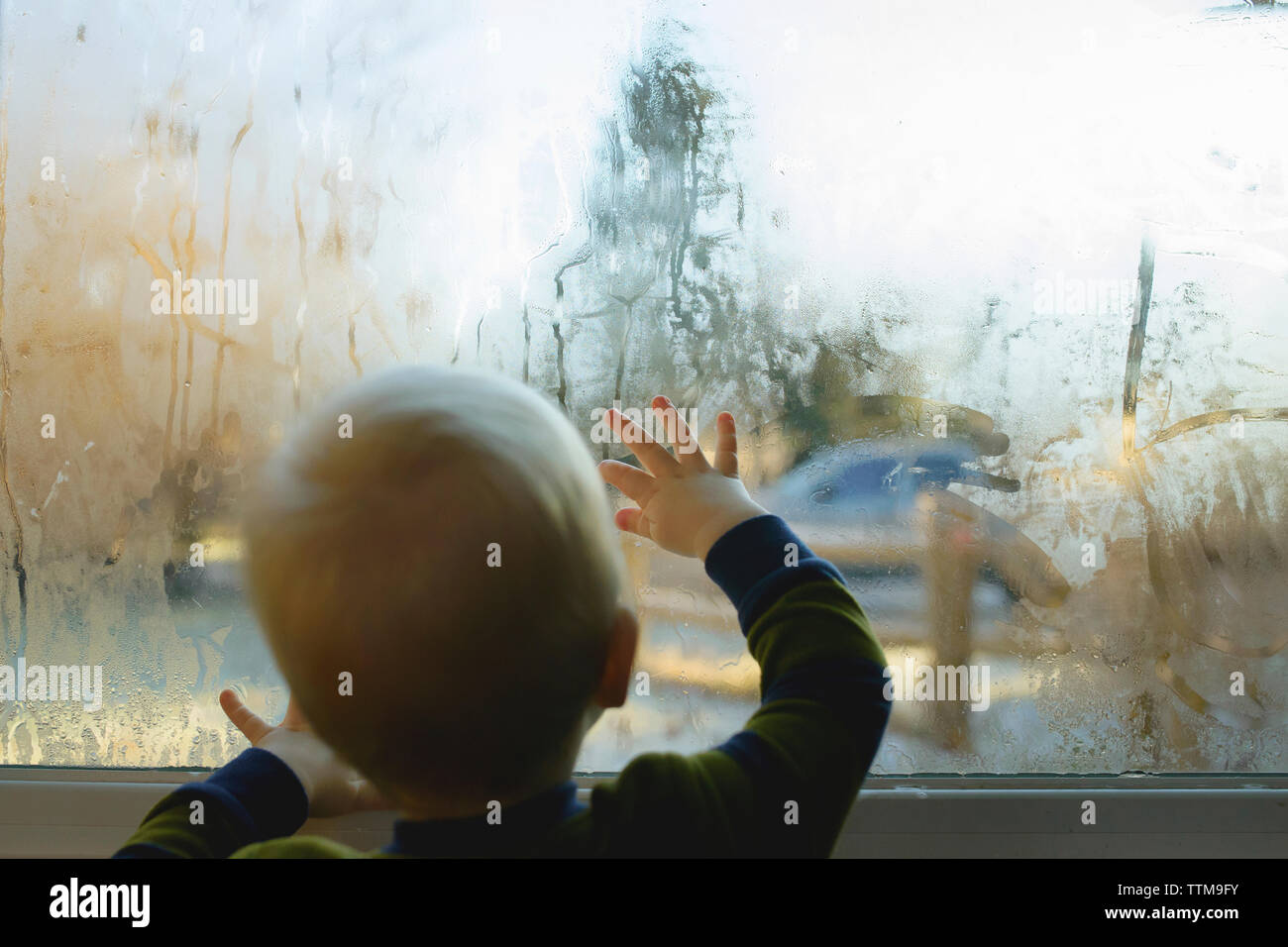 Rear view of boy looking through condensed glass window Stock Photo - Alamy
