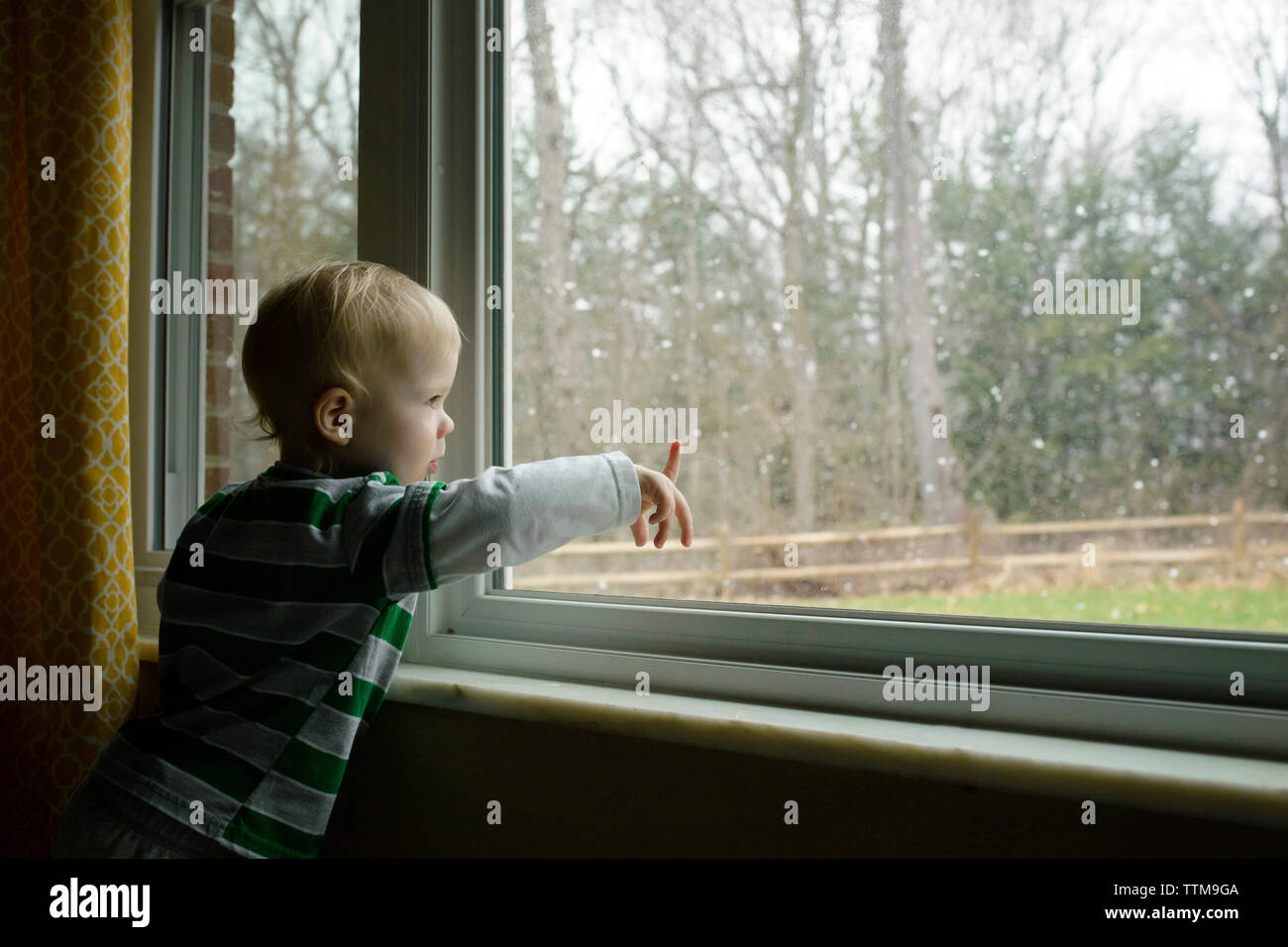 Boy looking through window while standing at home Stock Photo - Alamy