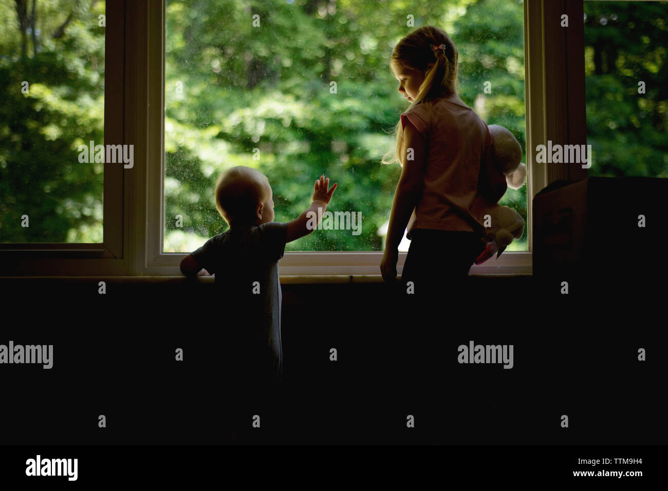 Girl looking at brother while standing by window Stock Photo - Alamy