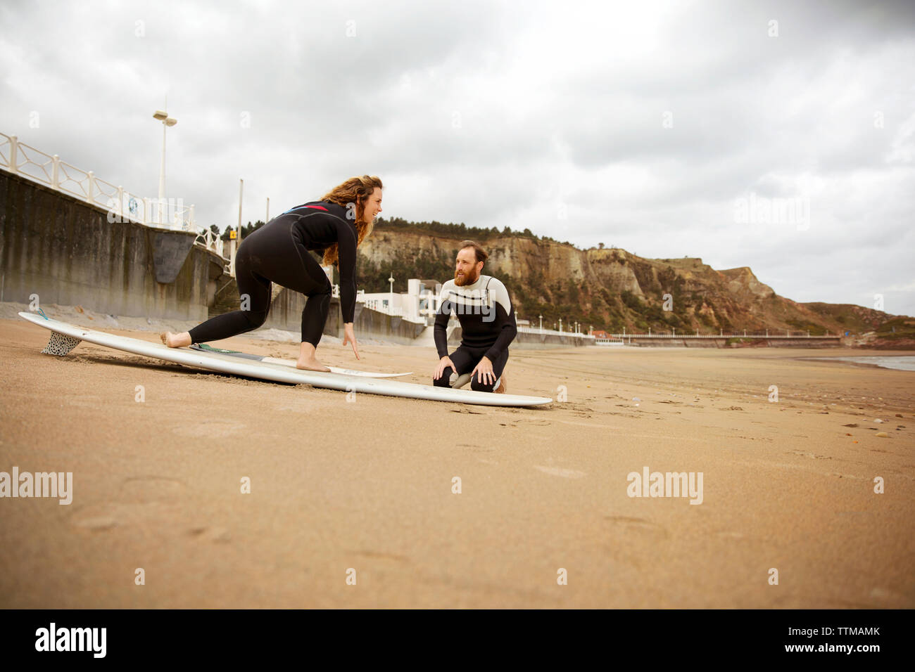 Man teaching surfing to woman at beach against cloudy sky Stock Photo ...