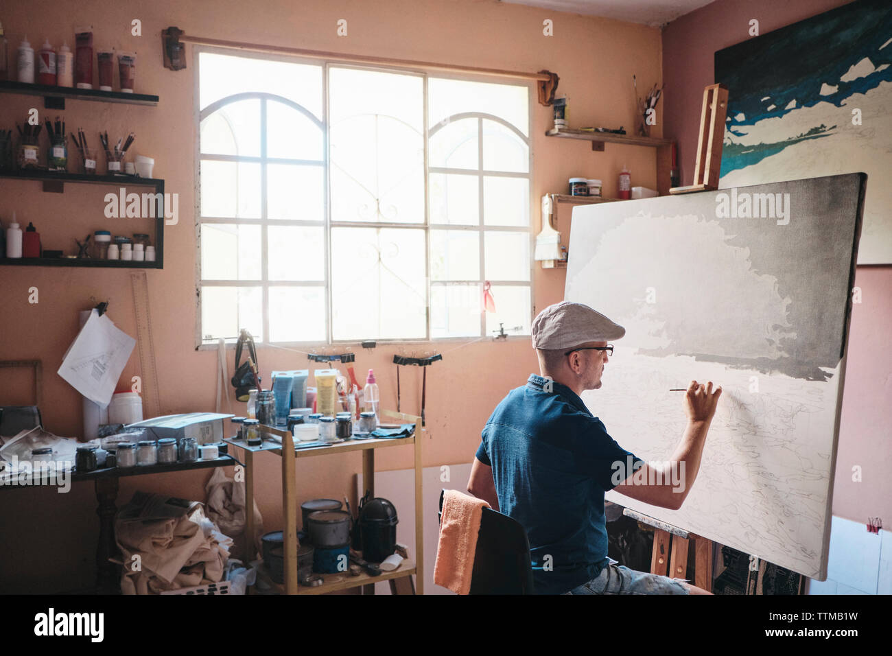 Mid adult Cuban artist painting with brush on canvas in his studio ...