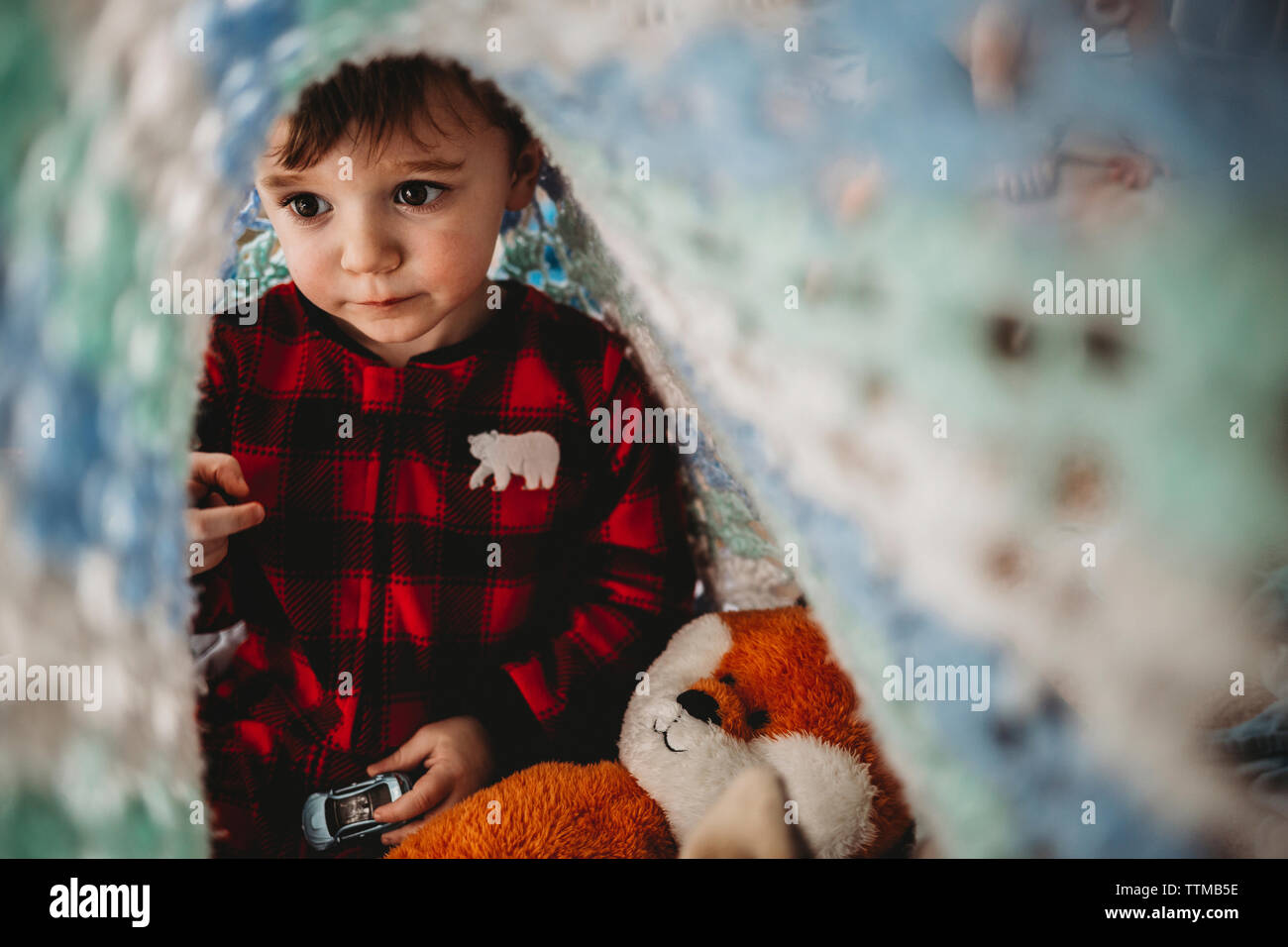 Boy playing with toys while sitting under blanket in bedroom Stock ...