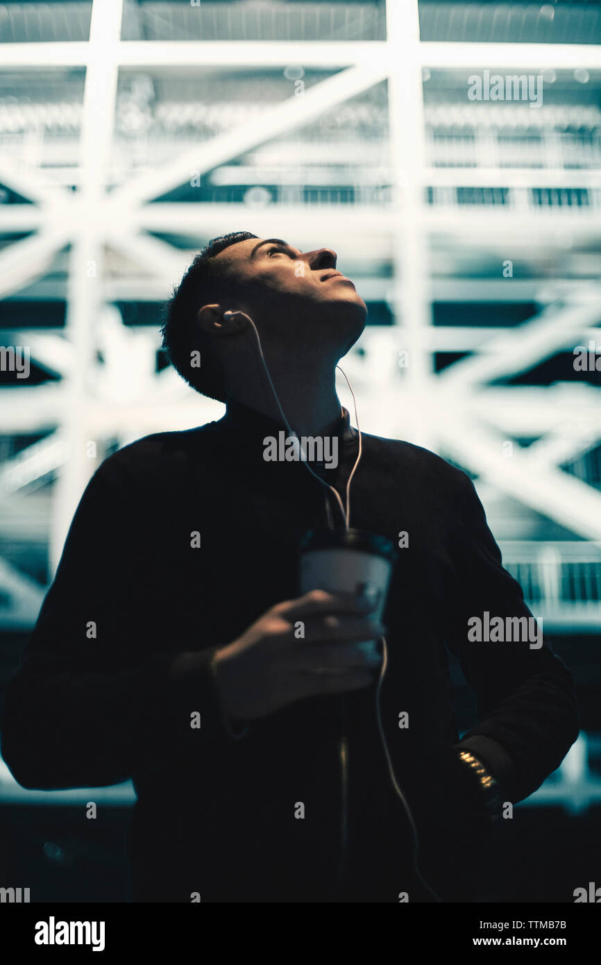 Young man with disposable cup listening music while standing against ...