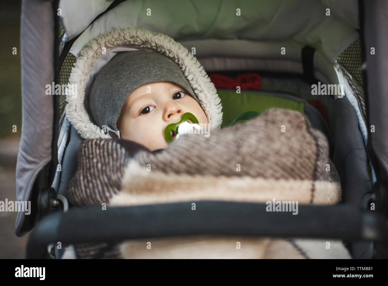 Portrait of cute toddler with pacifier in mouth lying on baby stroller ...